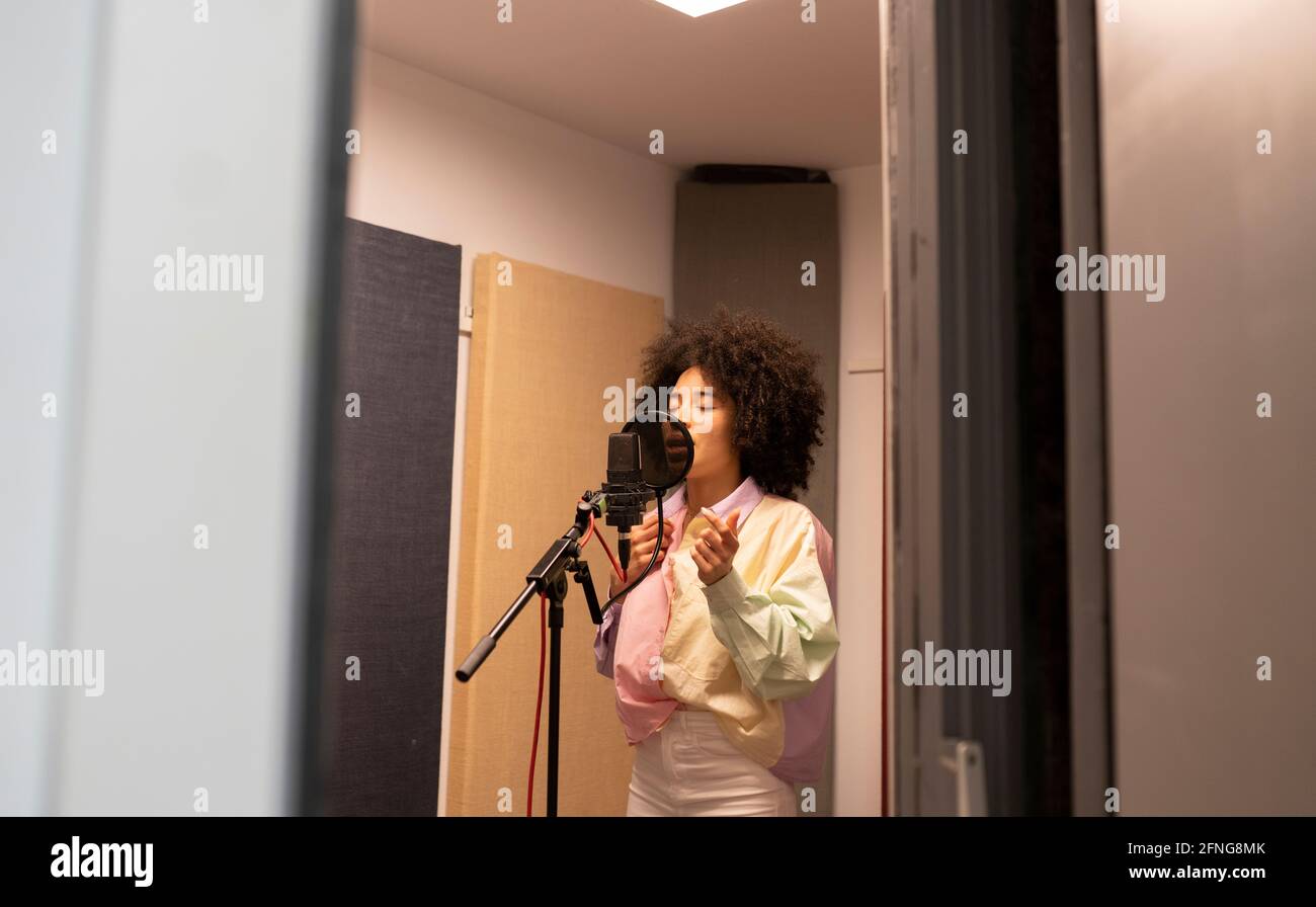 Black female singer performing song against microphone with pop filter ...