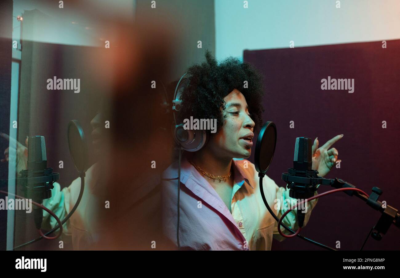 Black female singer performing song against microphone with pop filter ...