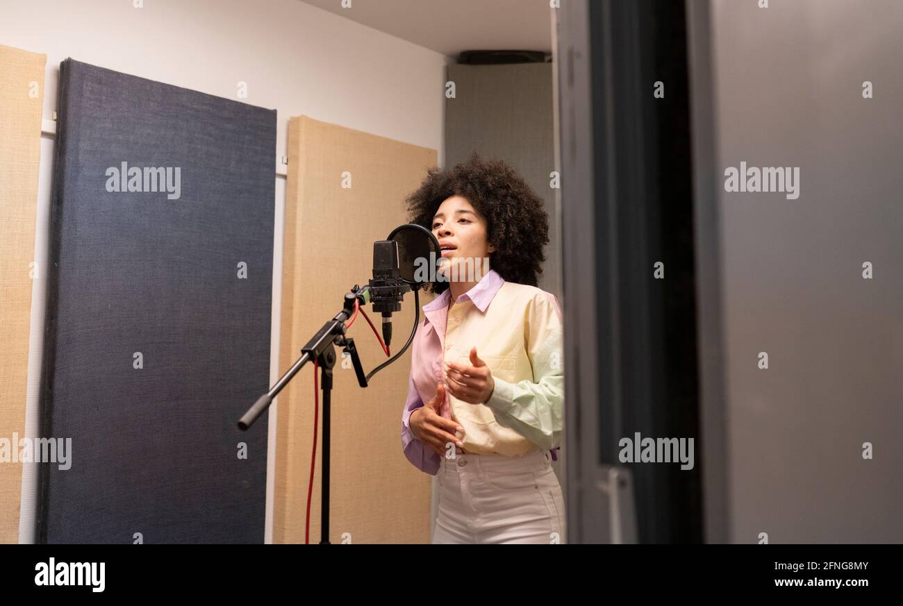 Black female singer performing song against microphone with pop filter ...