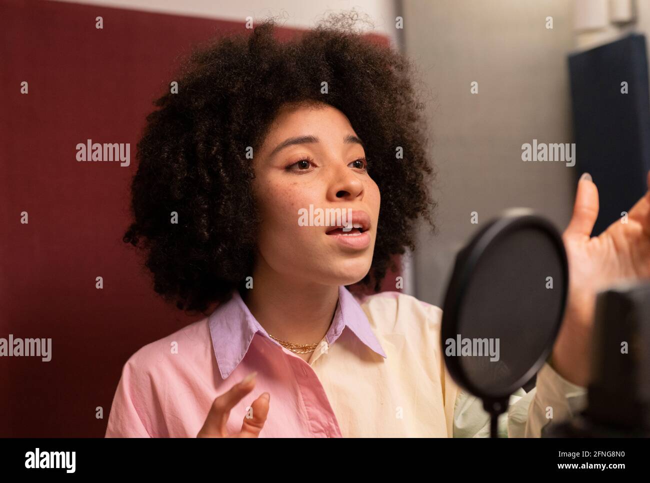 Black female singer performing song against microphone with pop filter ...