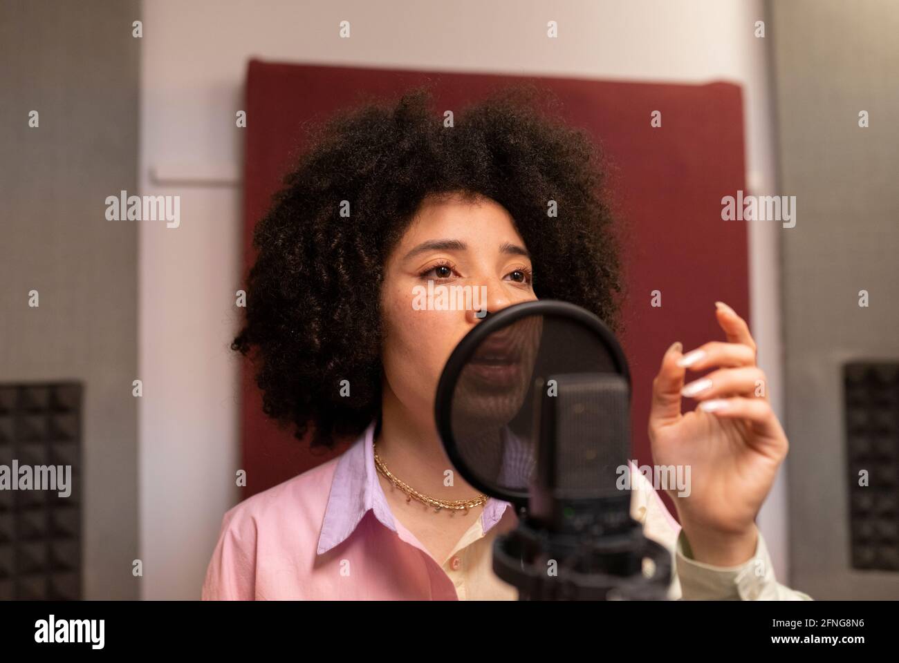 Black female singer performing song against microphone with pop filter ...