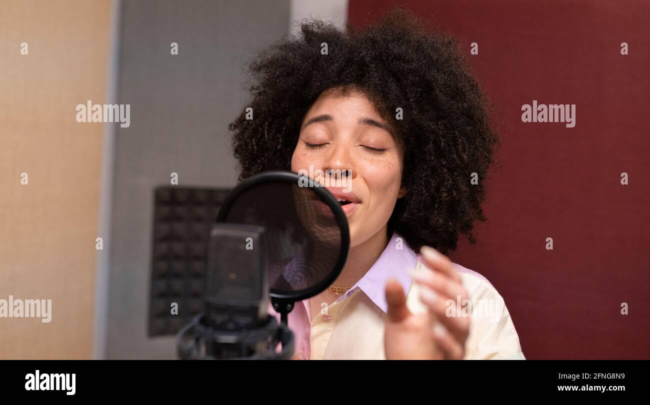 Black female singer performing song against microphone with pop filter ...