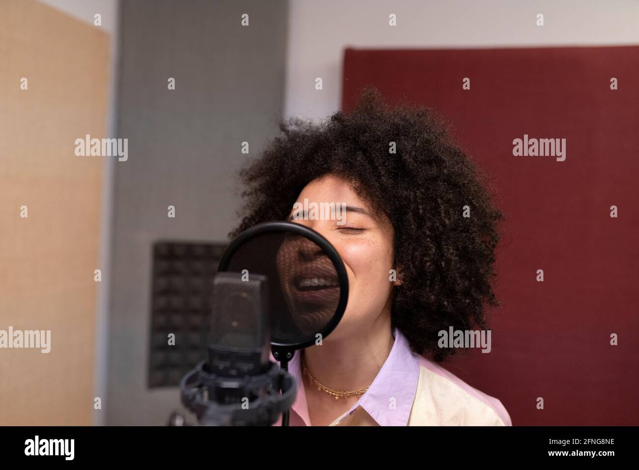 Black female singer performing song against microphone with pop filter ...