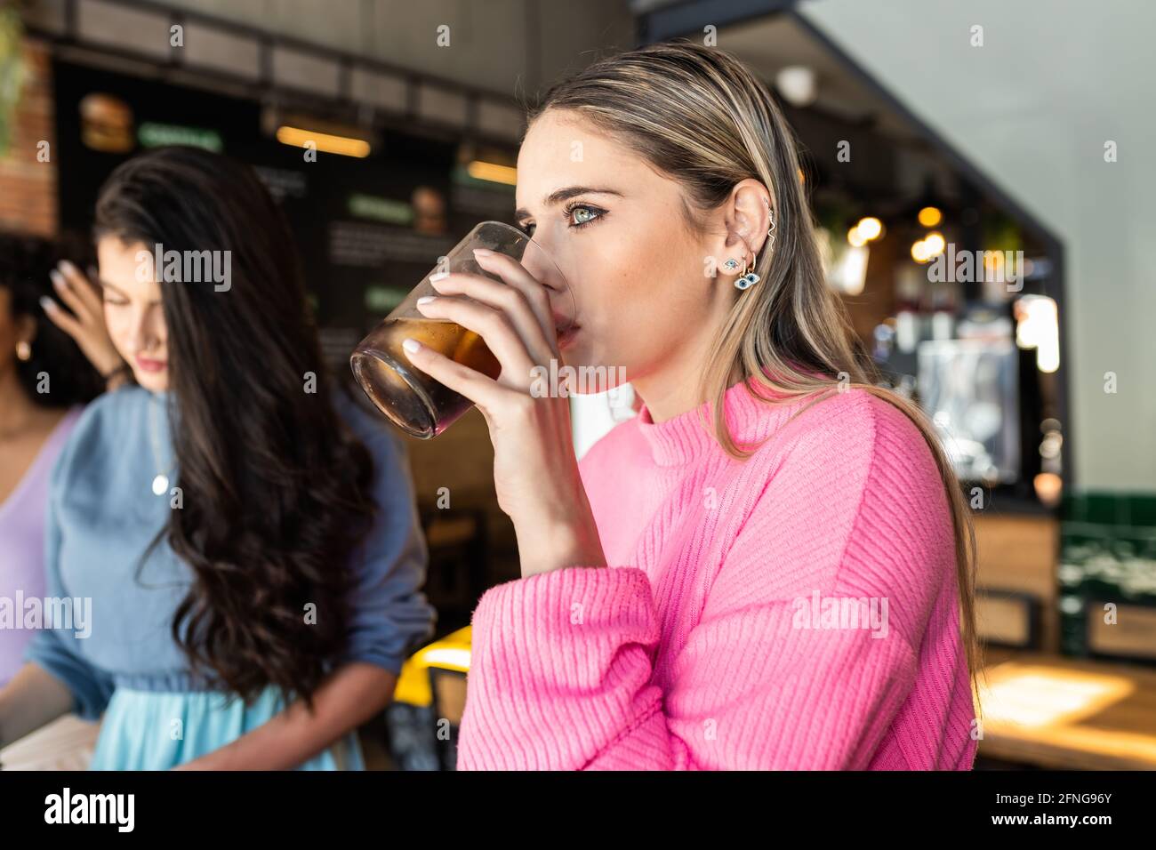 Side view of trendy young female in fashionable outfit drinking glass ...