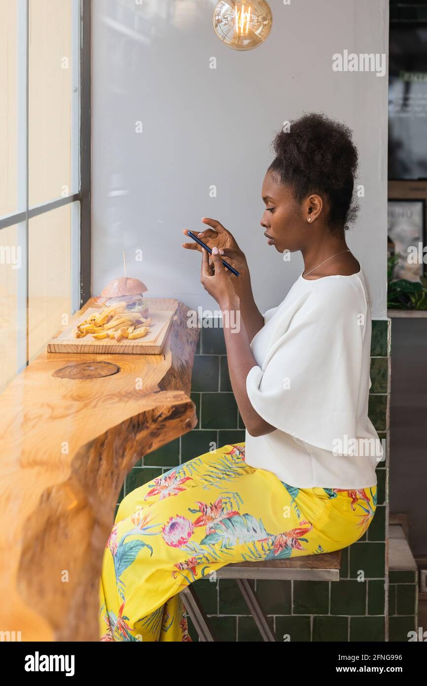Side view calm African American female in stylish wear taking pictures ...