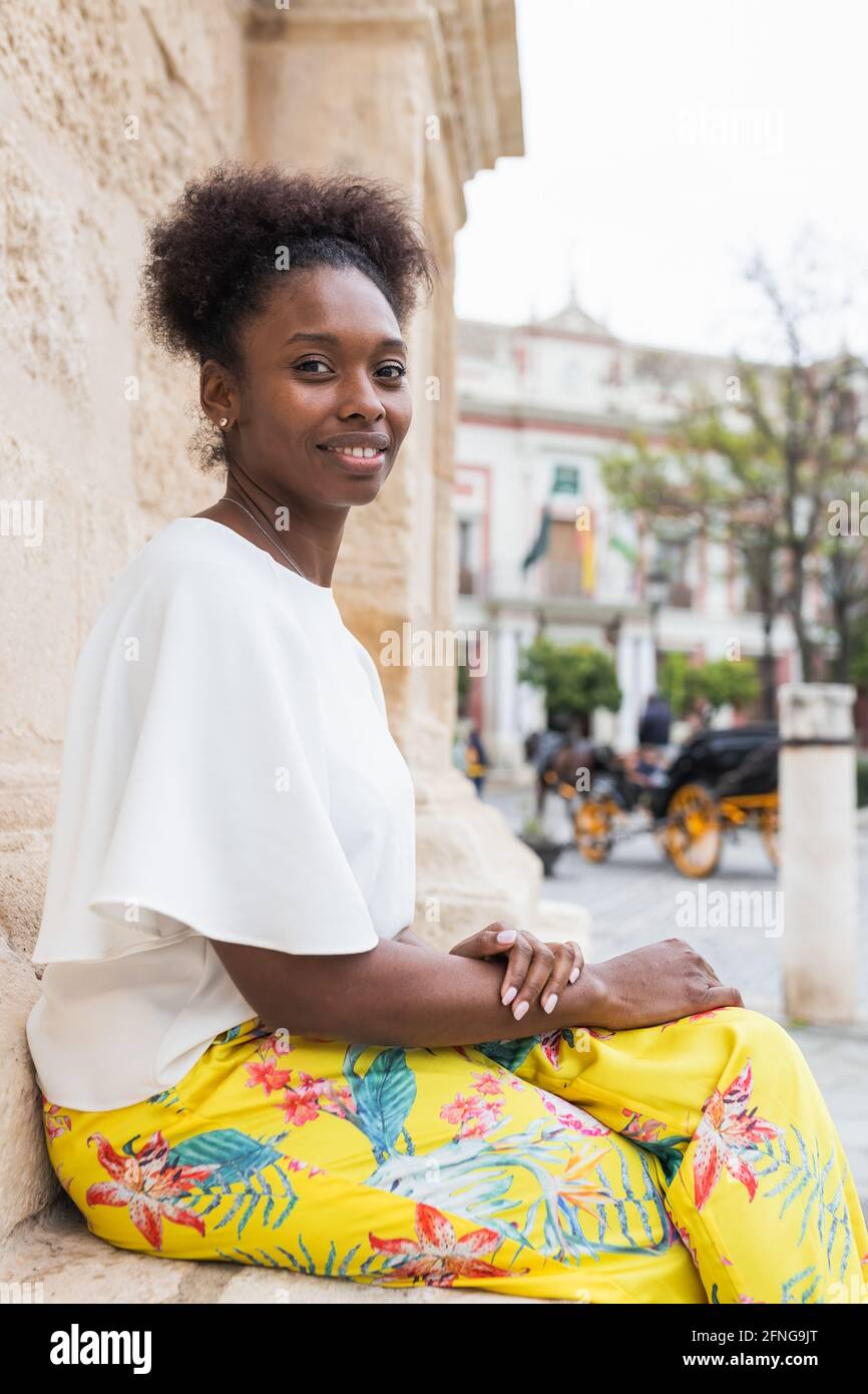 Side view smiling African American female in trendy outfit sitting with ...