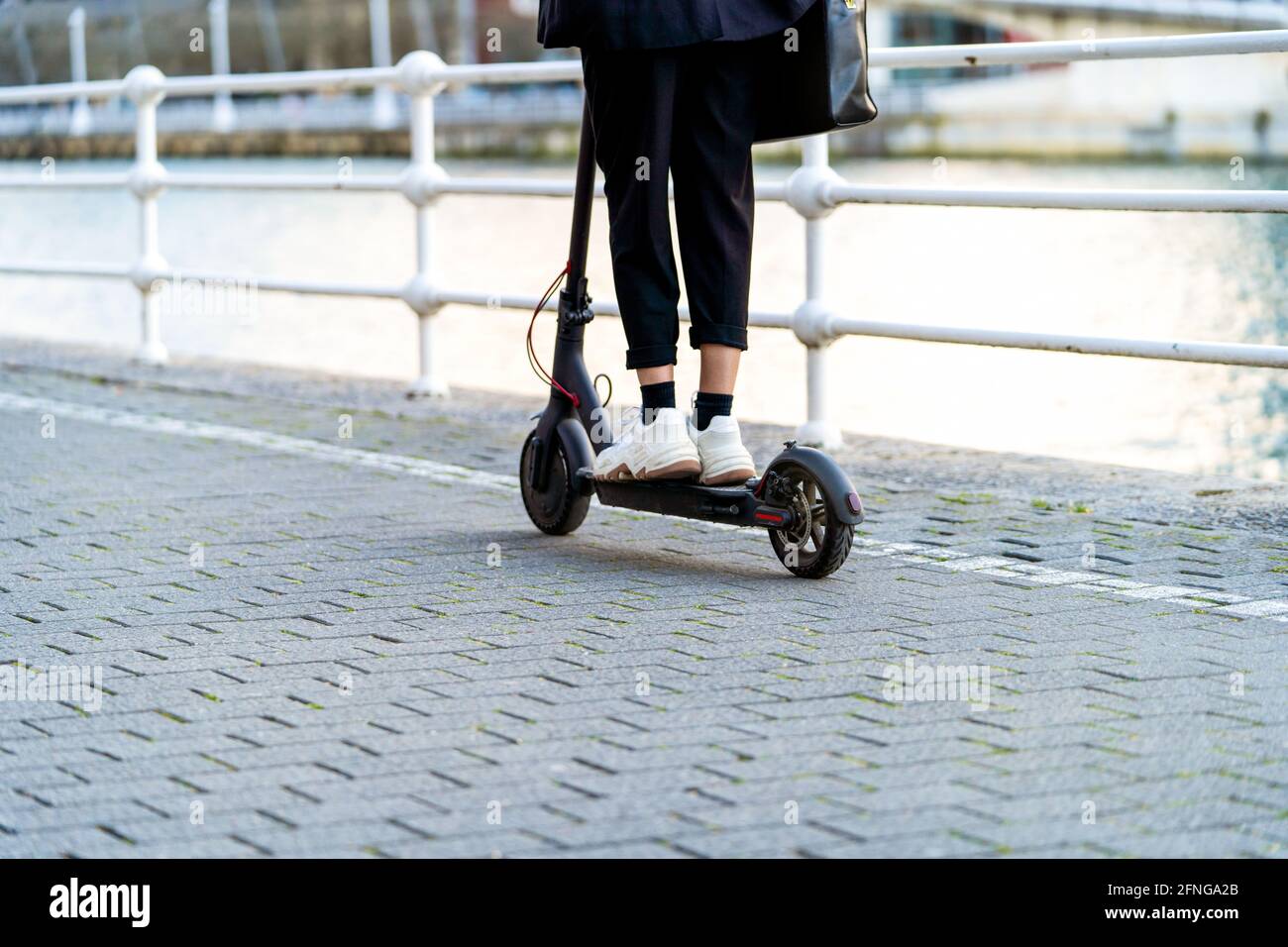 Side view of crop anonymous female in sneakers riding modern scooter on ...