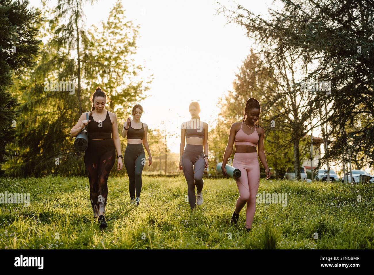 Confident fit multiracial female athletes walking with mat along lawn ...