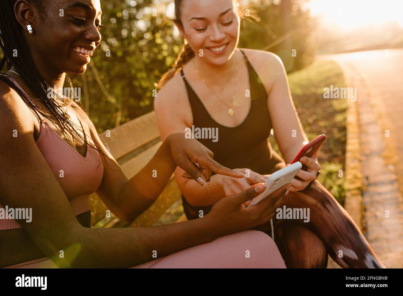 Cheerful multiracial female athletes in activewear sitting on bench in ...