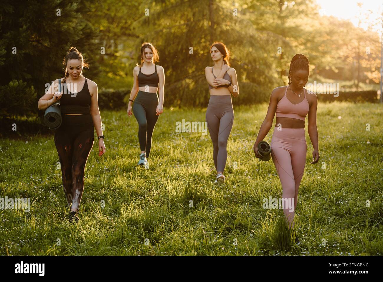 Confident fit multiracial female athletes walking with mat along lawn ...