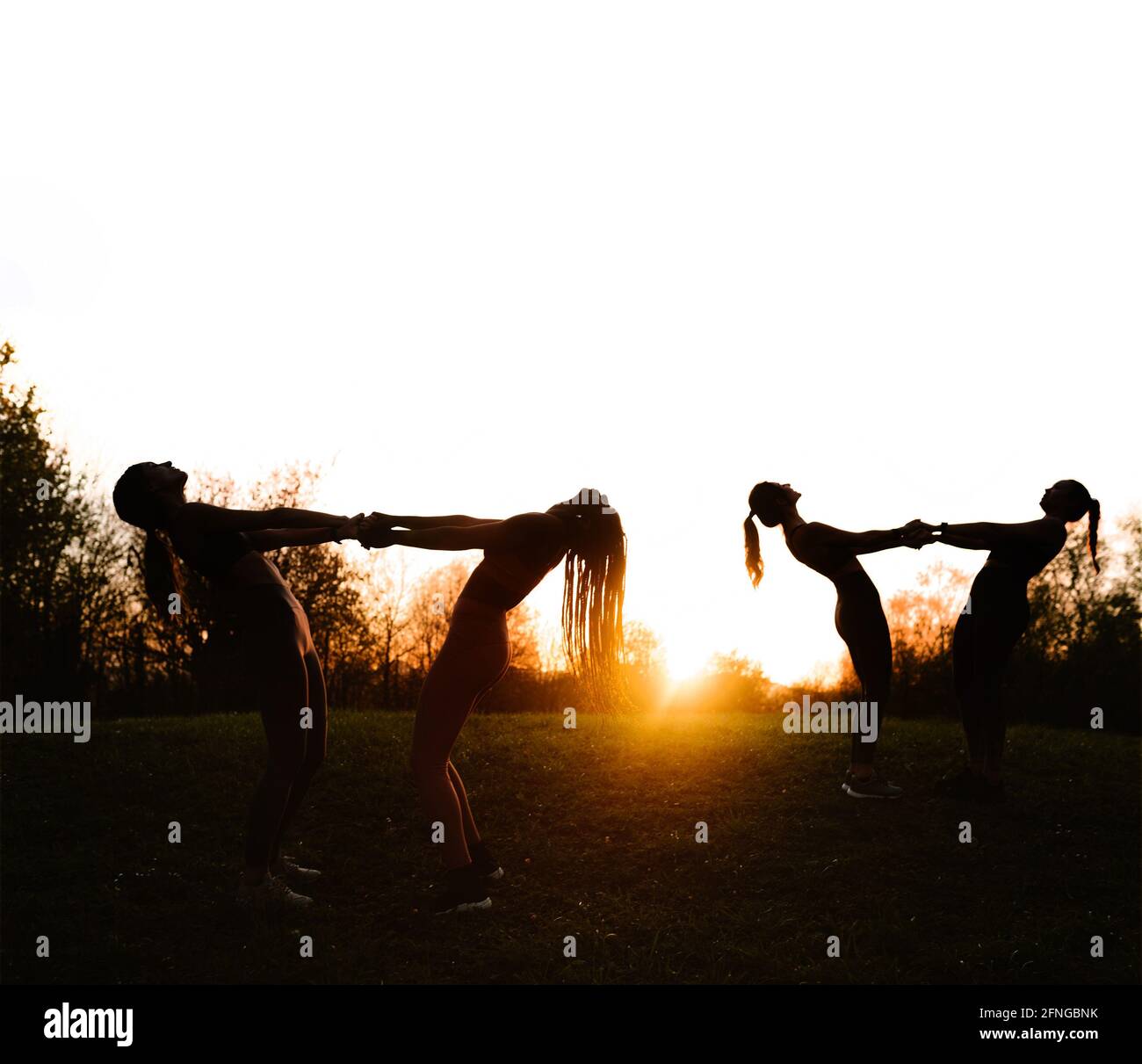 Side view of silhouettes of females practicing acro yoga together in ...