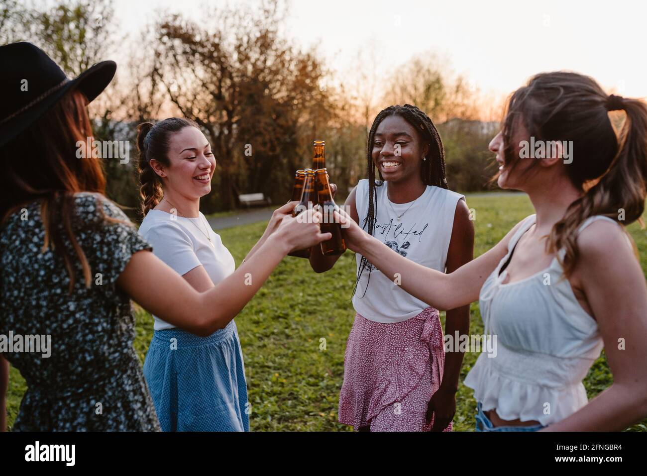 Group of happy diverse women gathering in park and clinking bottles of ...