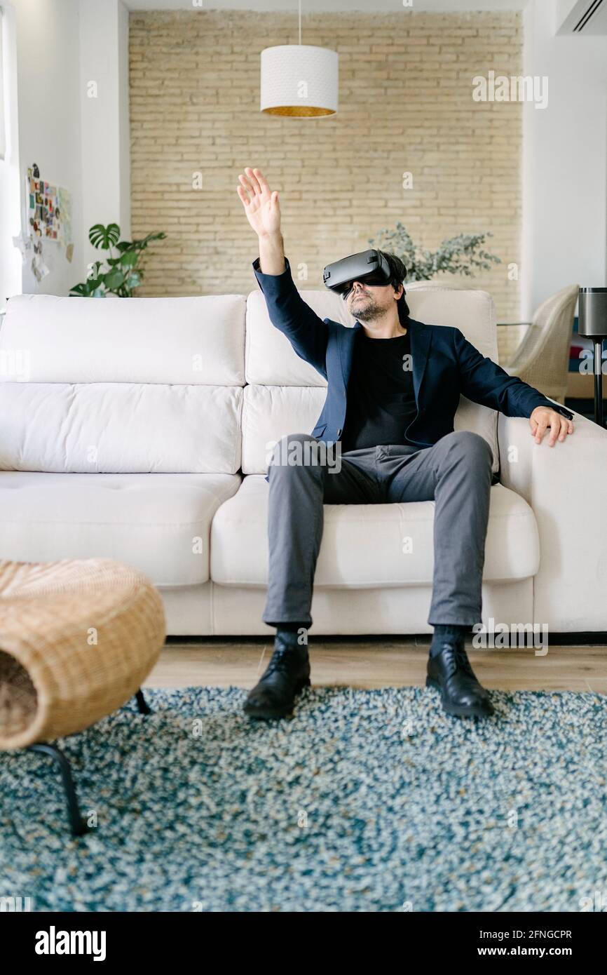 Adult man sitting on a modern sofa experiencing virtual reality in the ...