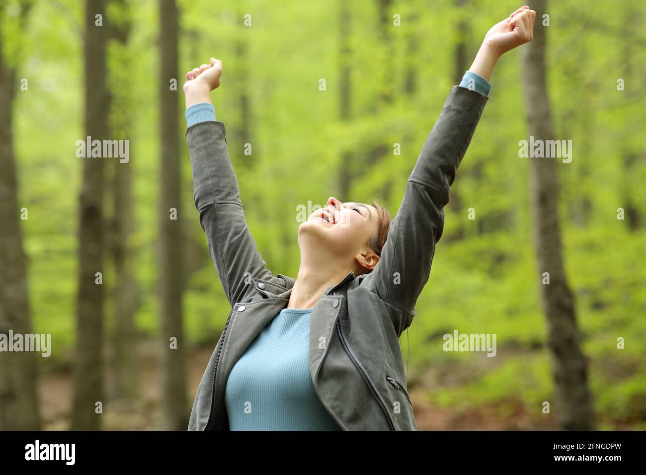 Excited woman celebrating spring season raising arms in a green forest ...