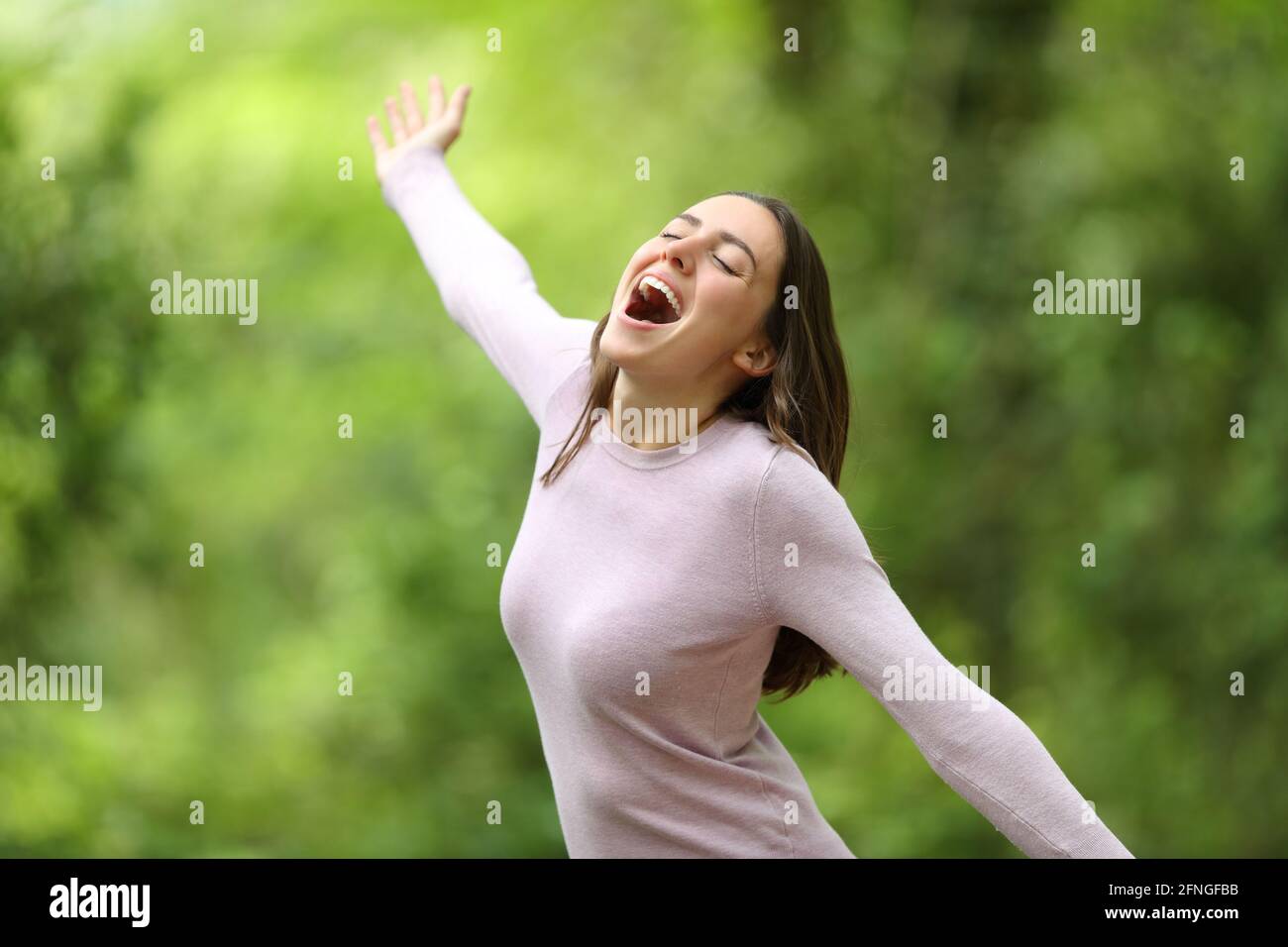 Excited woman screaming spreading stretching arms in a forest or park ...