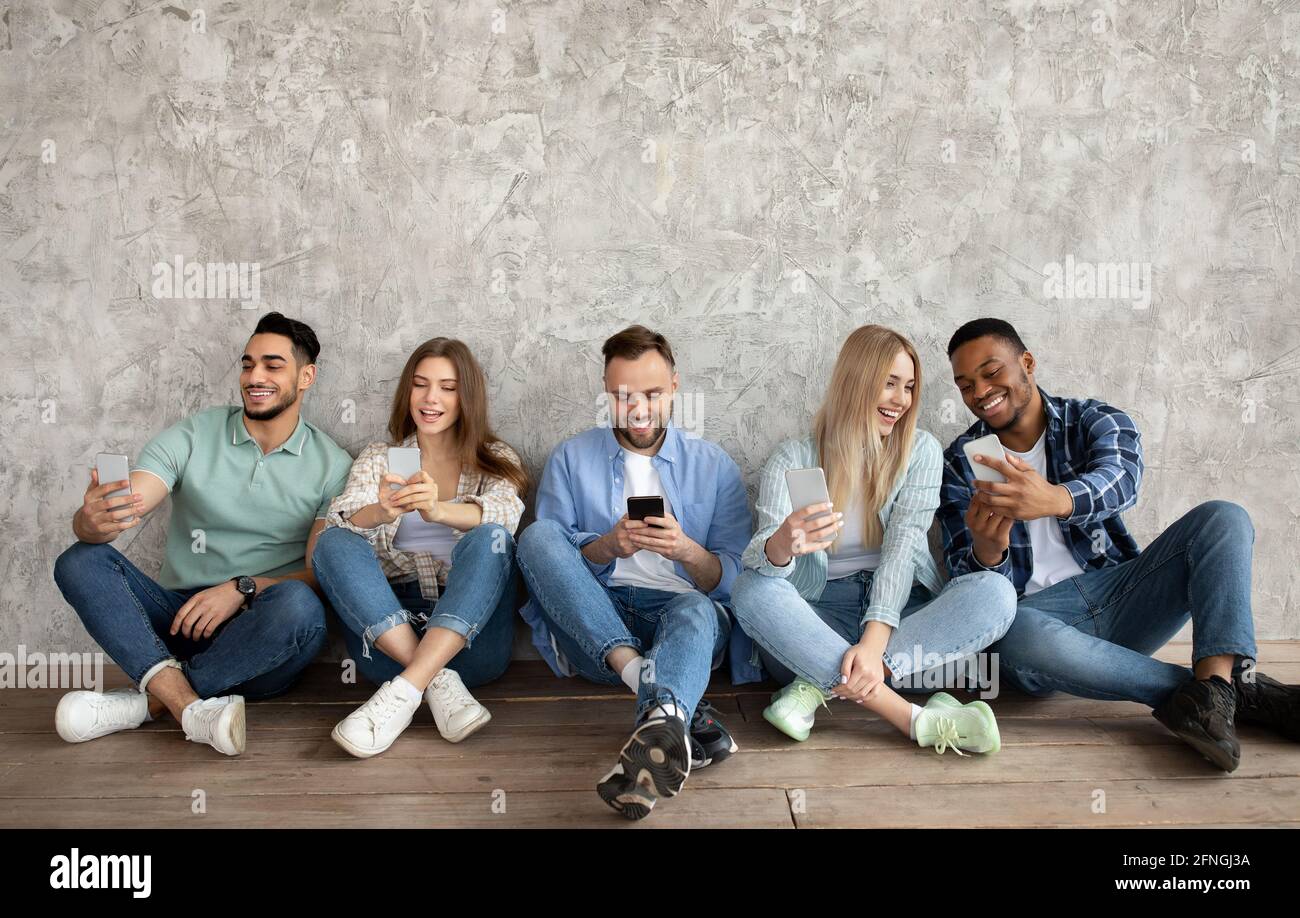 Full length of millennial students with modern smartphones sitting near ...