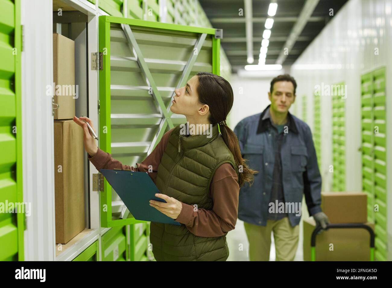 Young woman checking boxes with man carrying them in the background ...