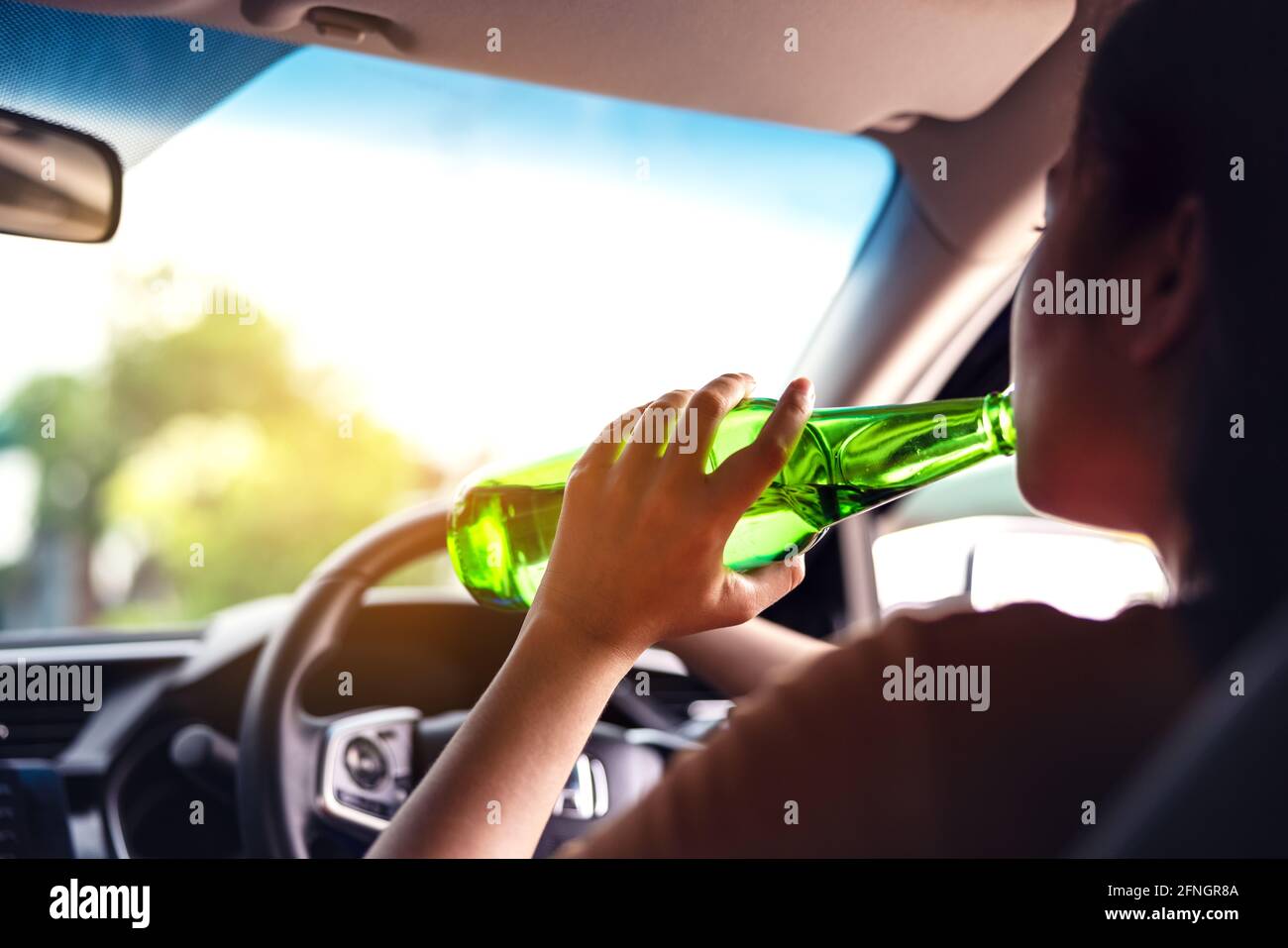 woman drinking from a beer bottle while driving car, a concept of ...