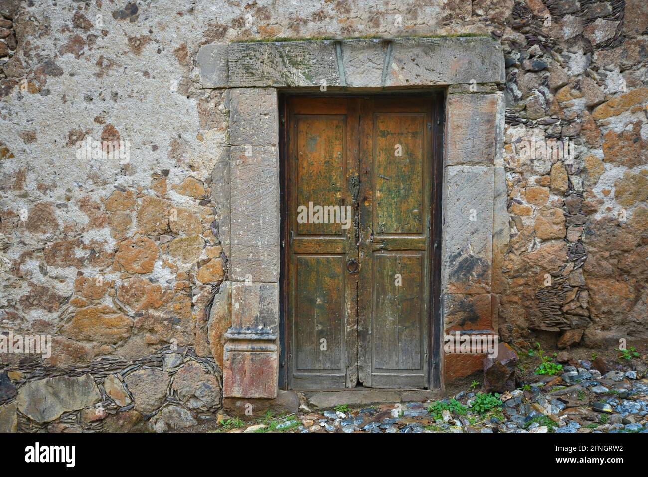 Old abandoned house facade with a handcrafted stone wall and a weathered wooden door in the ...