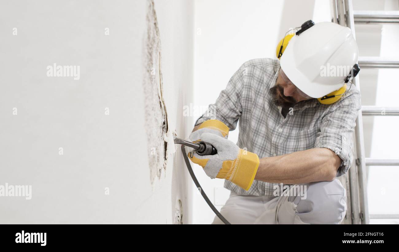 house renovation concept, construction worker breaks the old plaster of ...
