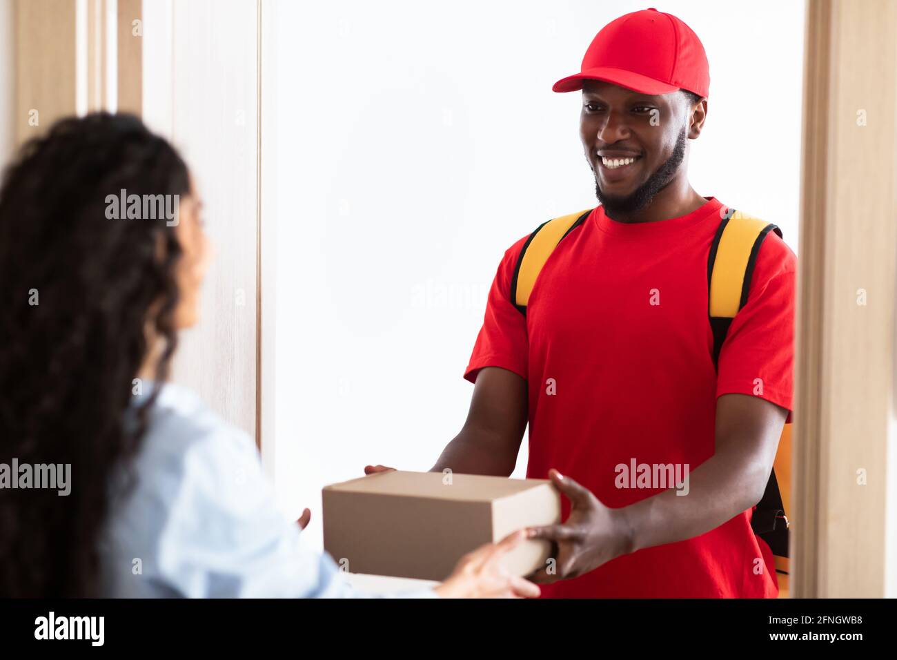 Black delivery man holding box giving it to customer Stock Photo - Alamy