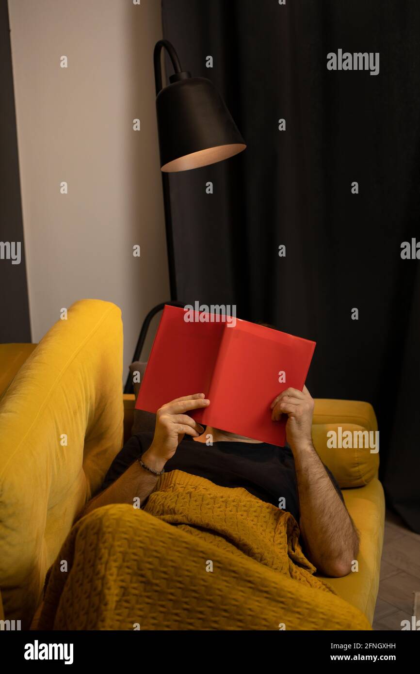 hairy arms guy reads book liyng on comfortable yellow sofa covered with ...