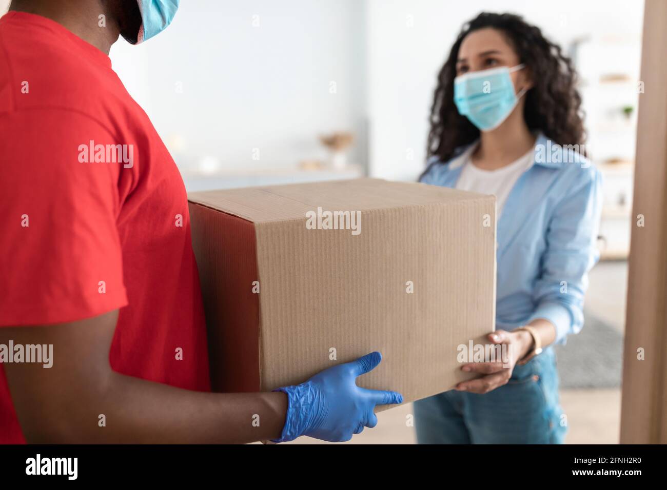 Black delivery man in medical mask giving box to woman Stock Photo - Alamy