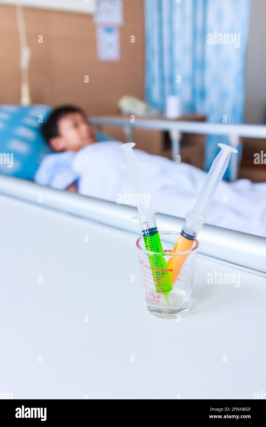 Syringes in a glass measuring cup with blurred illness boy lying on ...