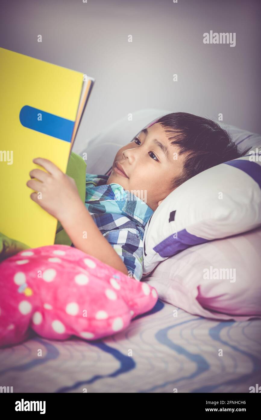 Handsome asian boy reading a book lying on bed in bedroom. Children ...