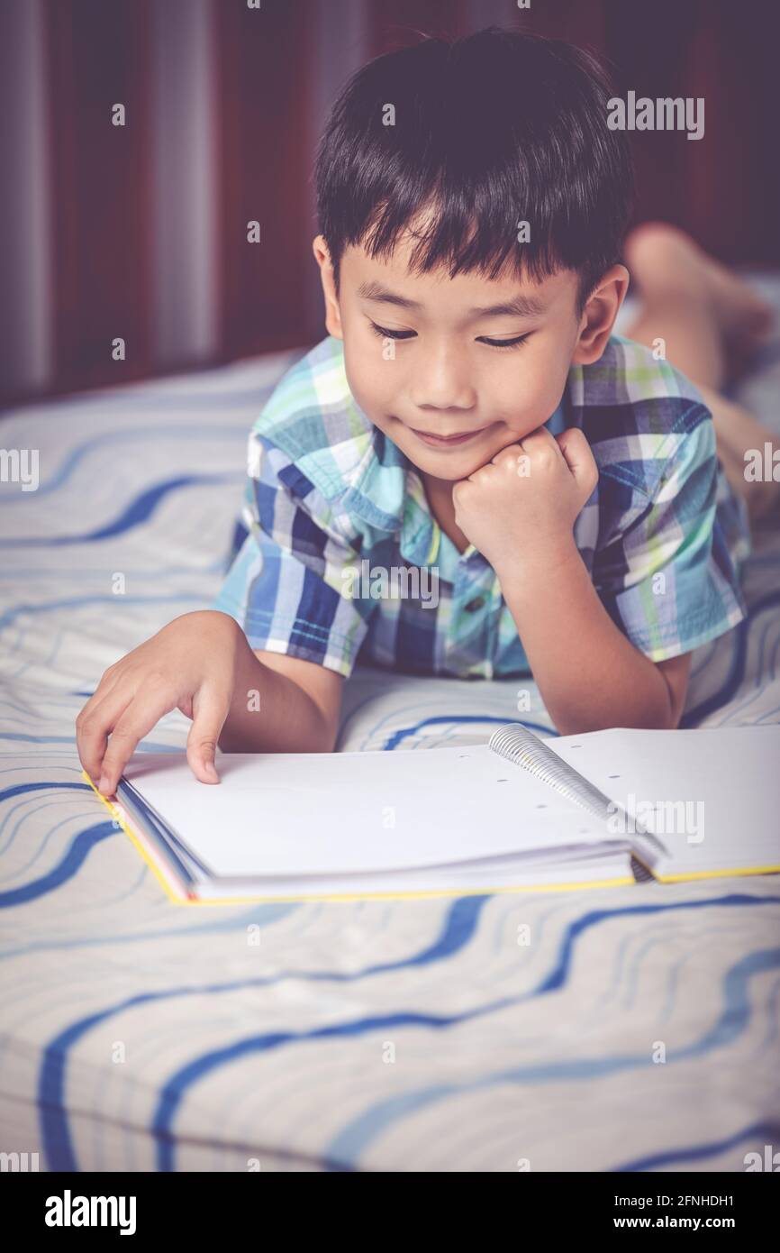 Handsome asian child reading a book lying down on bed in bedroom ...