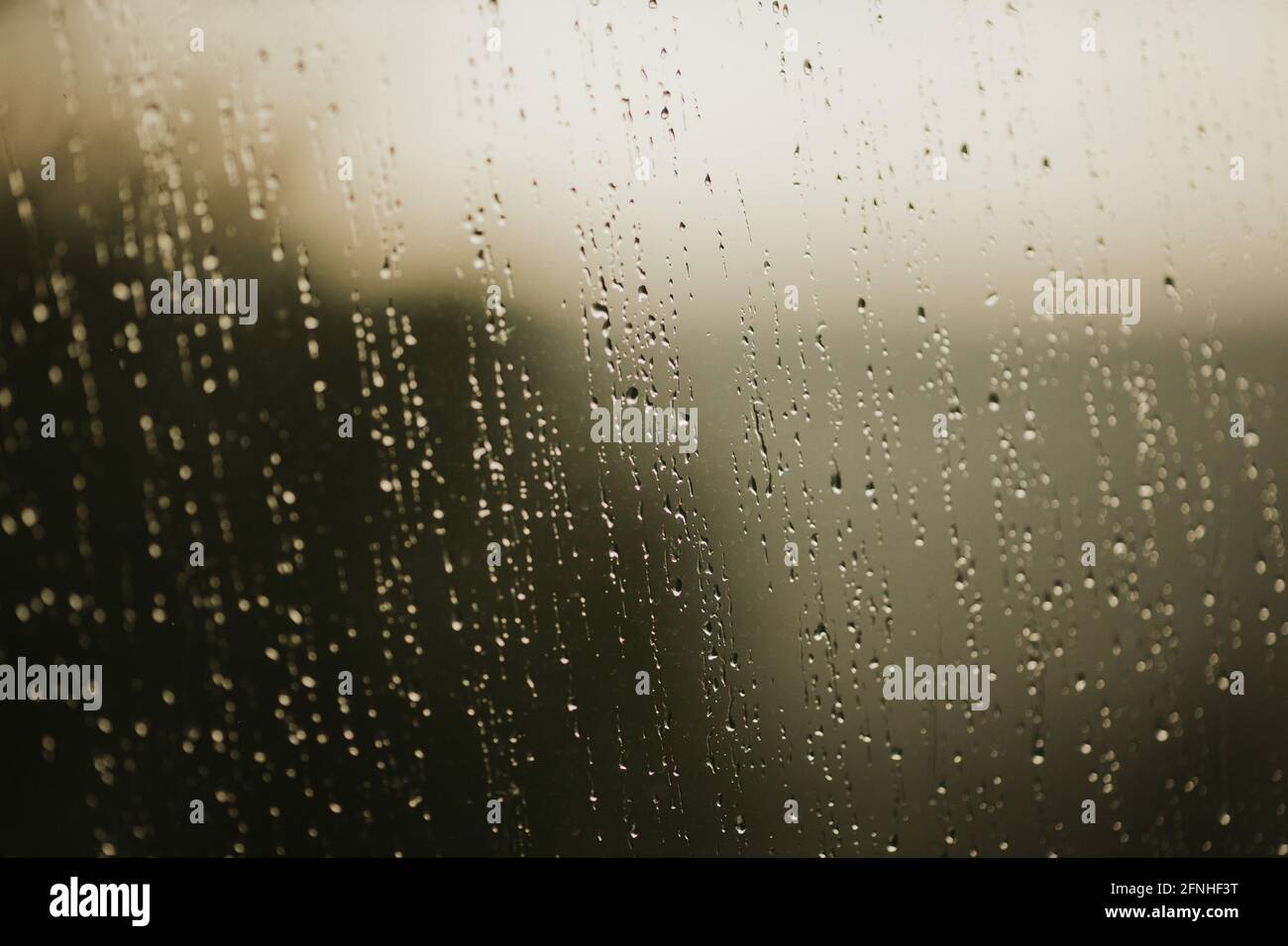 Blurry shot of a glass window covered with raindrops and a dimly lit ...