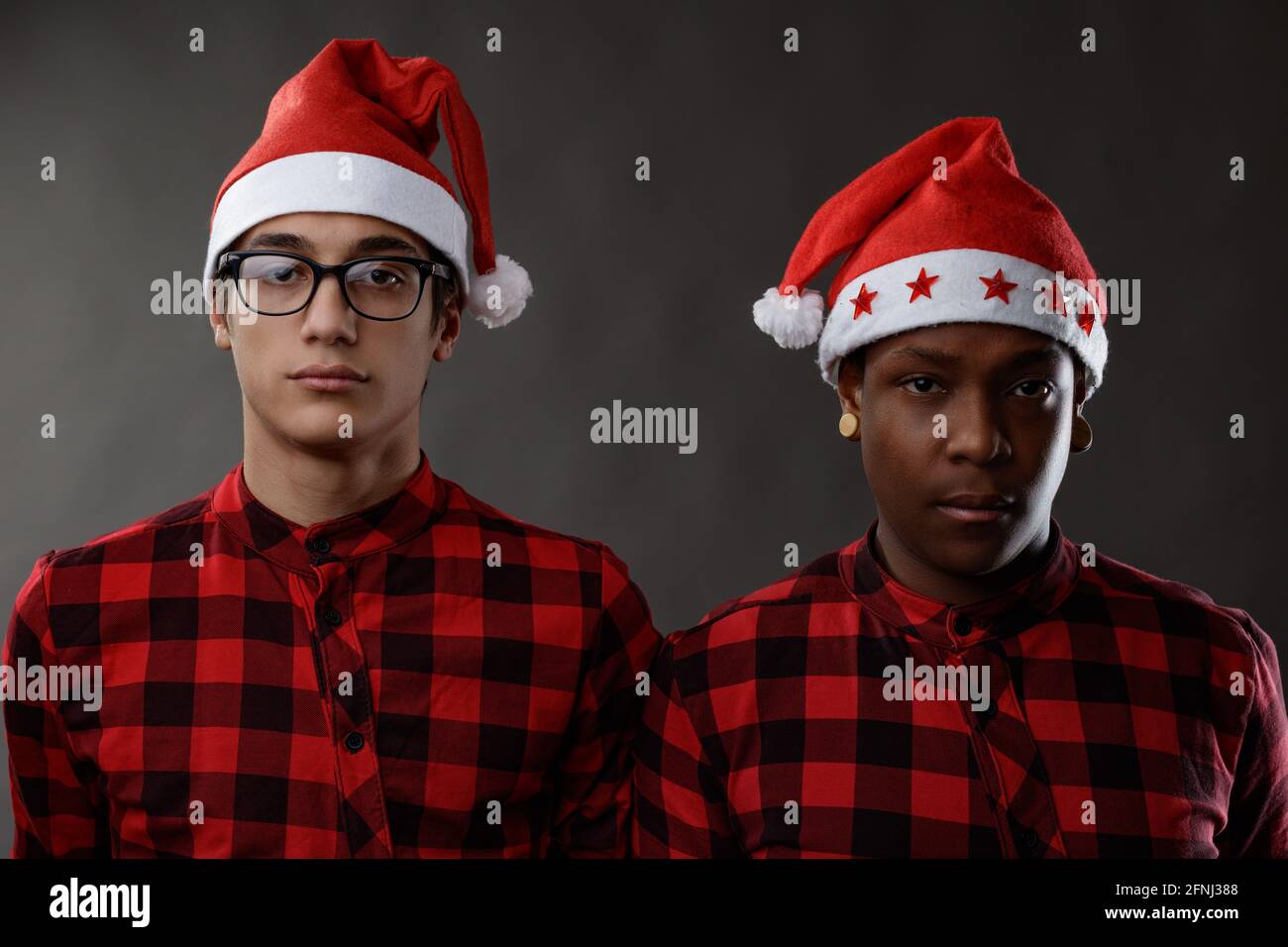 Two sombre young men wearing red Santa hats for Christmas posing side ...