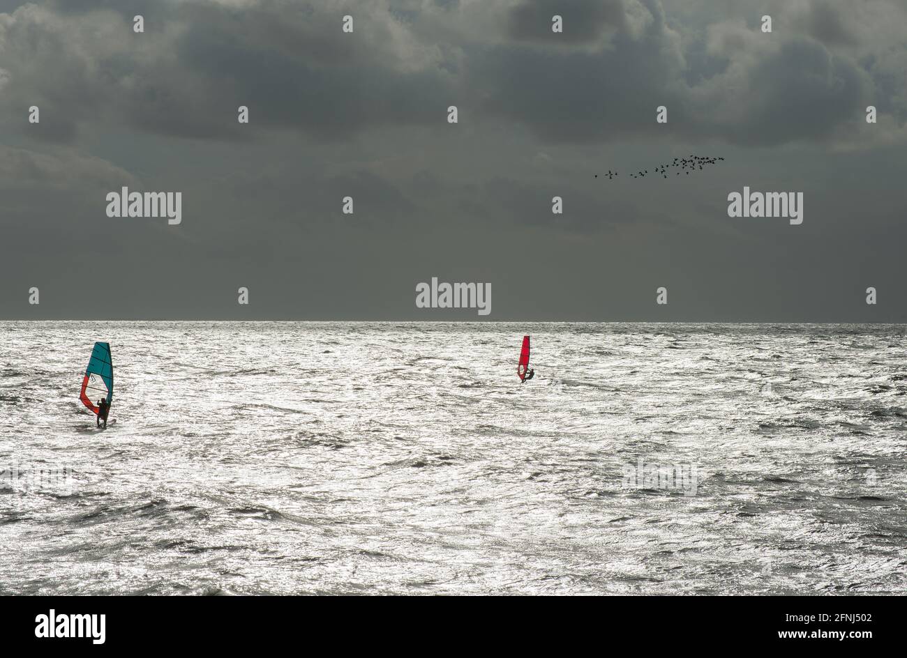 Stunning image of two windsurfers catching the sun, one with a blue ...