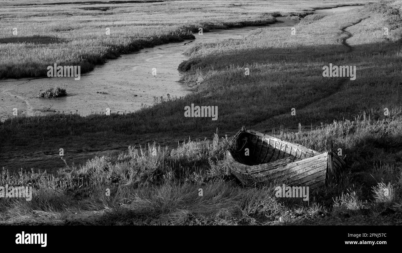 Mono image of a rotting and abandoned rowing boat drawn up from a sea ...