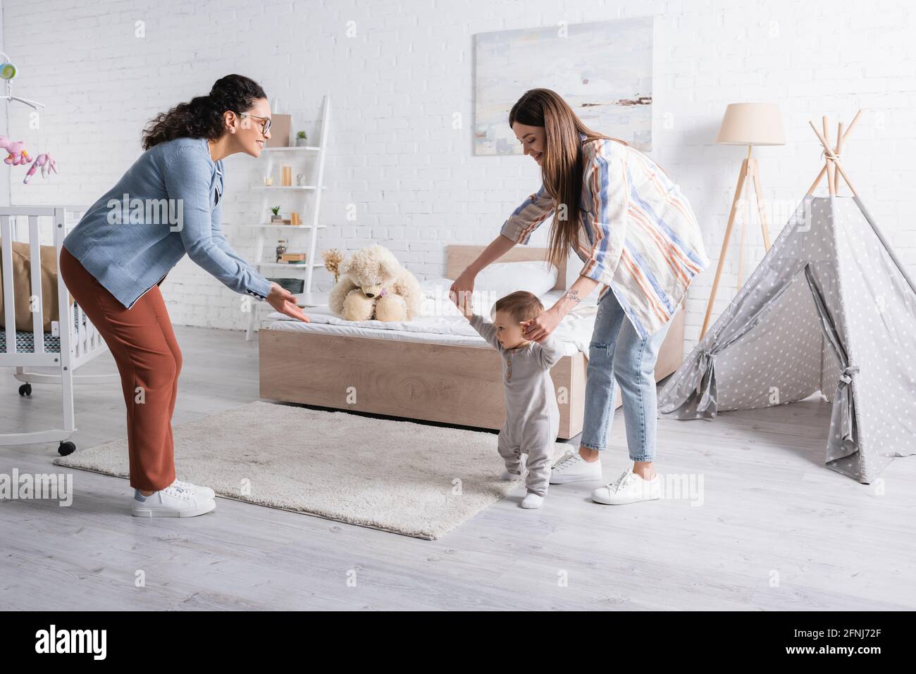mother supporting baby boy walking near smiling african american woman ...