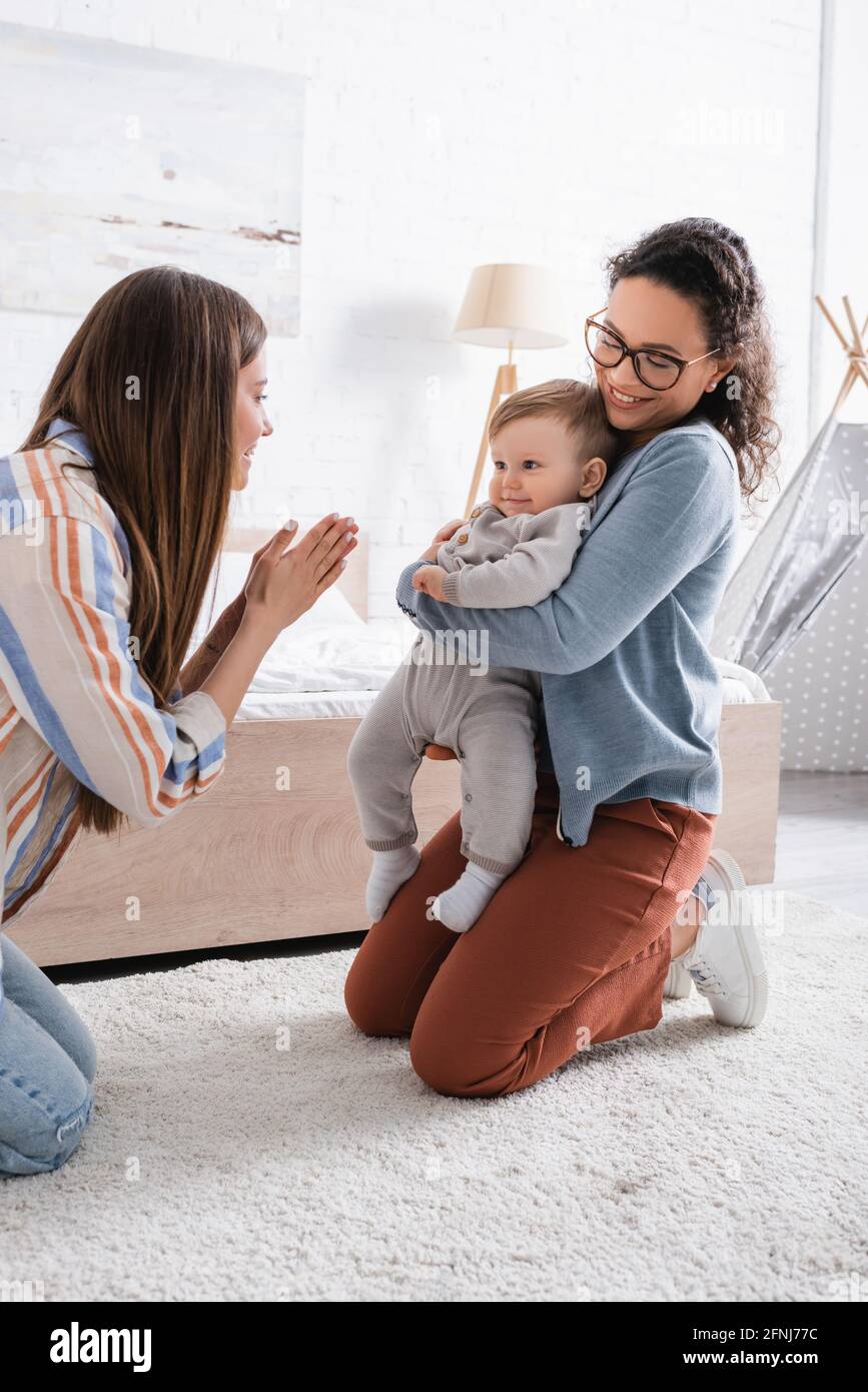 smiling african american woman in glasses holding baby boy near caring ...