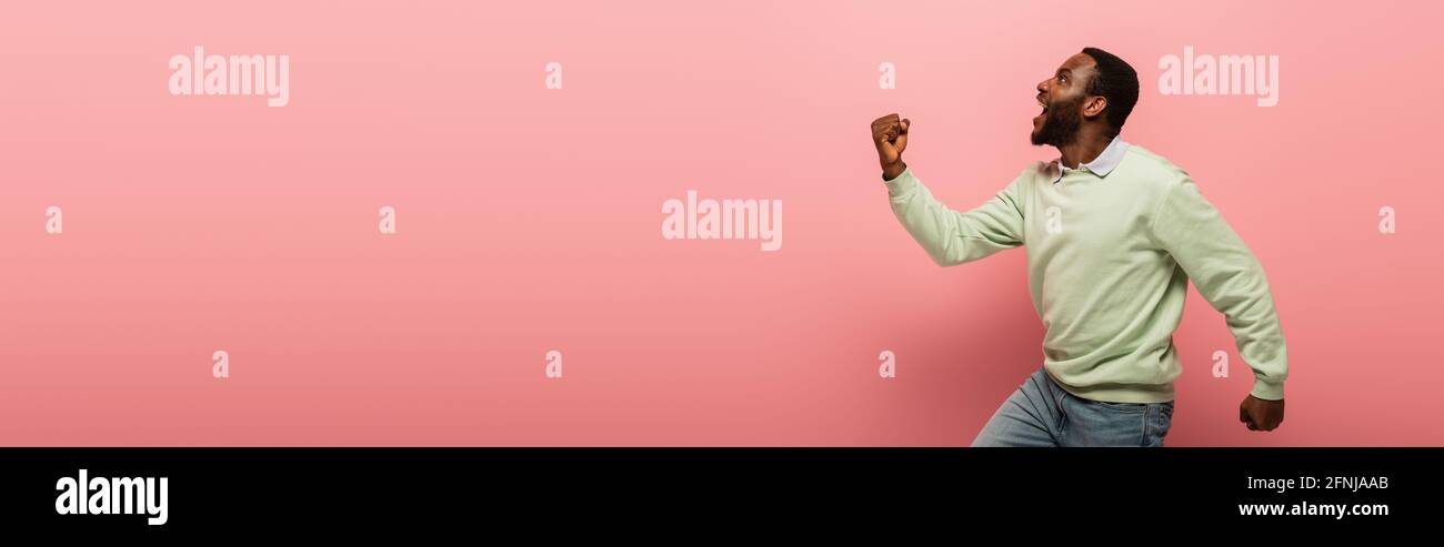 Side view of amazed african american man showing yeah gesture on pink ...