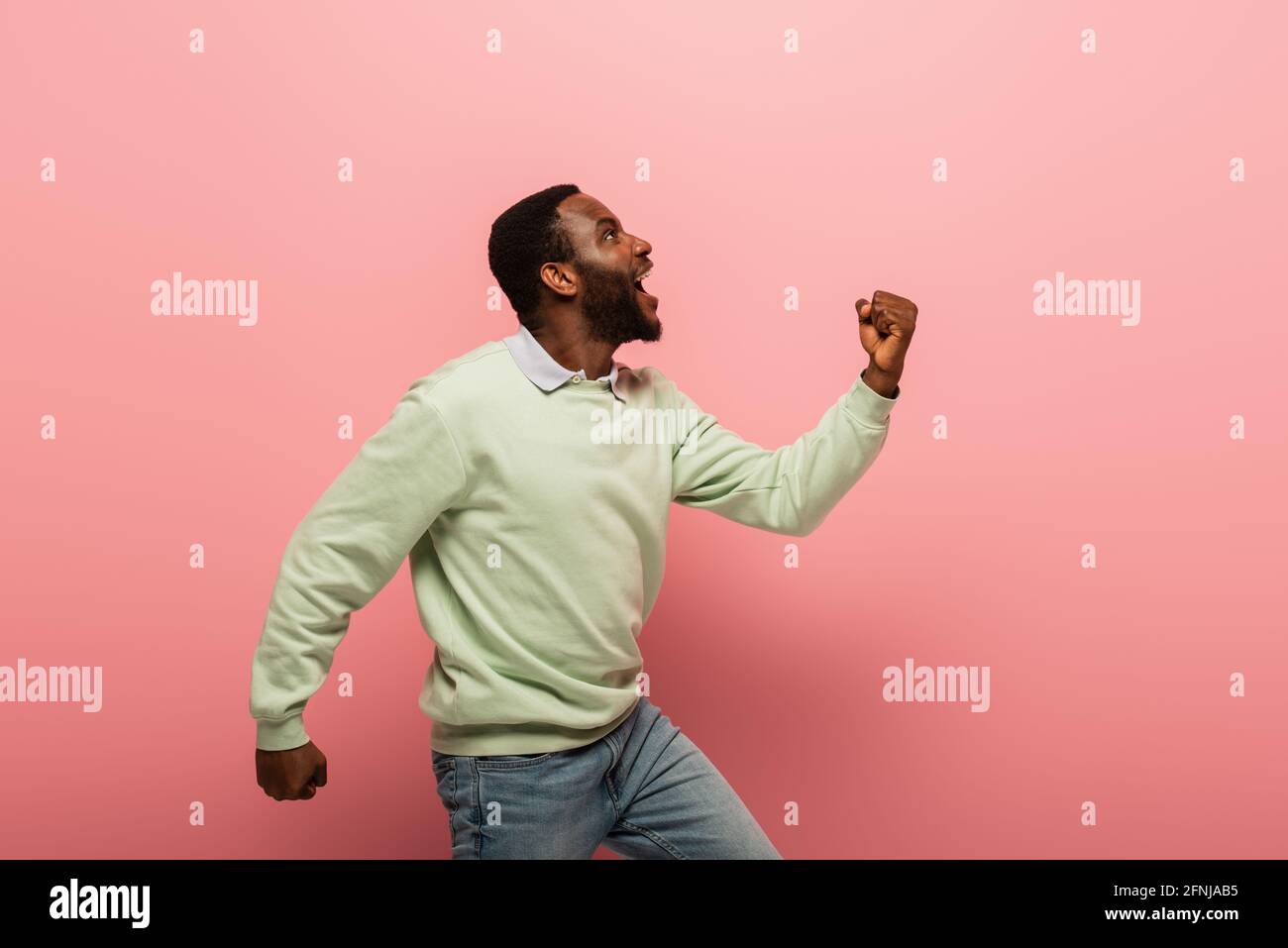 Side view of excited african american man showing yeah gesture on pink ...