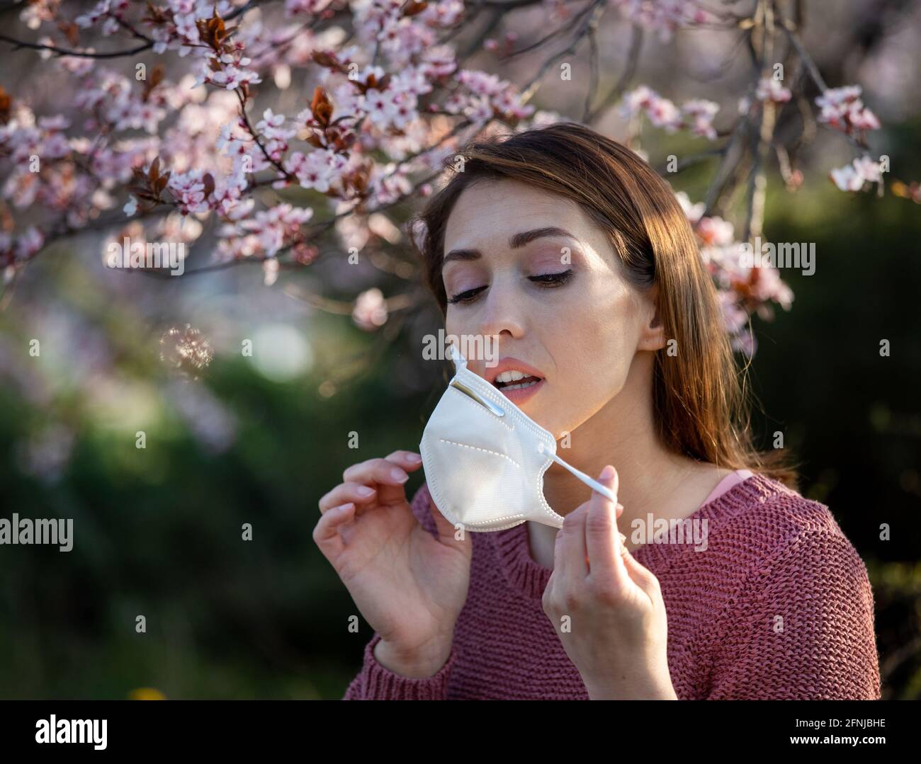 Smiling young woman putting facial mask on and looking at blooming tree ...