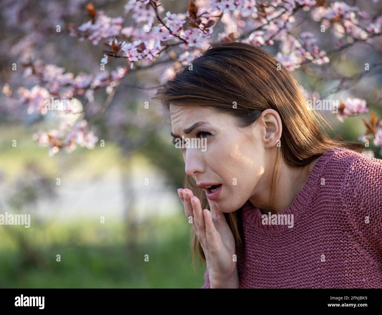 Pretty young woman sneezing in front of blooming tree. Spring allergy ...