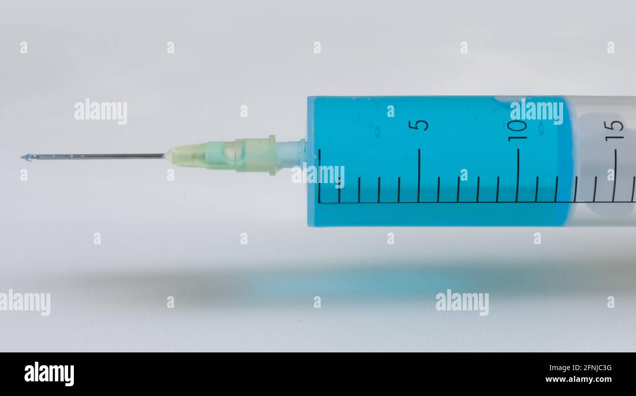 Close-up of a plastic injection syringe with needle filled with a blue ...