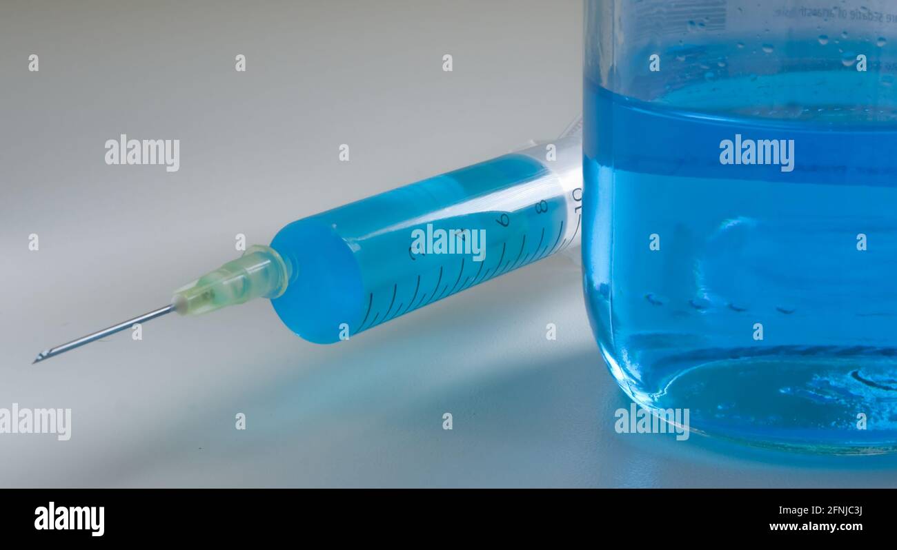 Large syringe with needle next to a bottle of blue injection fluid ...