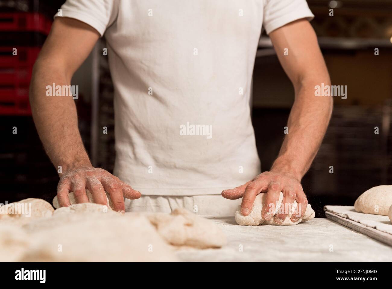 young male baker in bakery factory manually kneading fresh bread knead ...