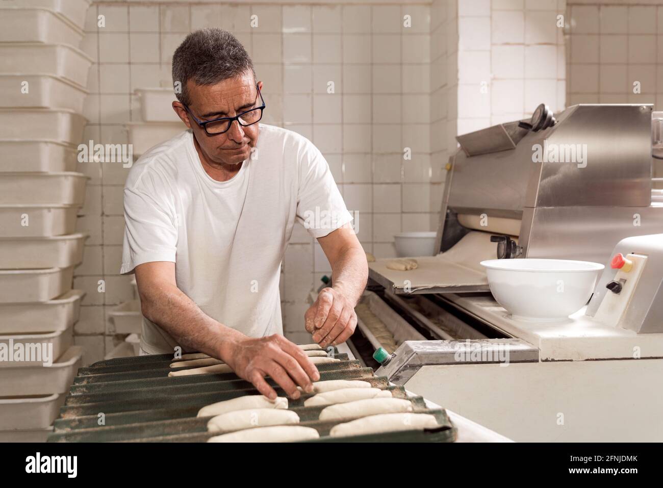 old authentic baker in bakery making organic bread and taking care of ...
