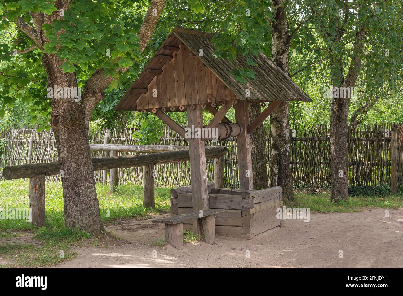 A rural well with a bench in the shade of branching trees. Stock Photo ...
