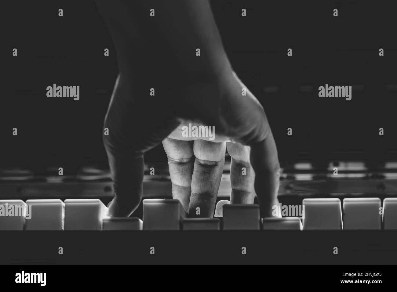 A woman's single hand is playing piano, touching keys in a low light ...