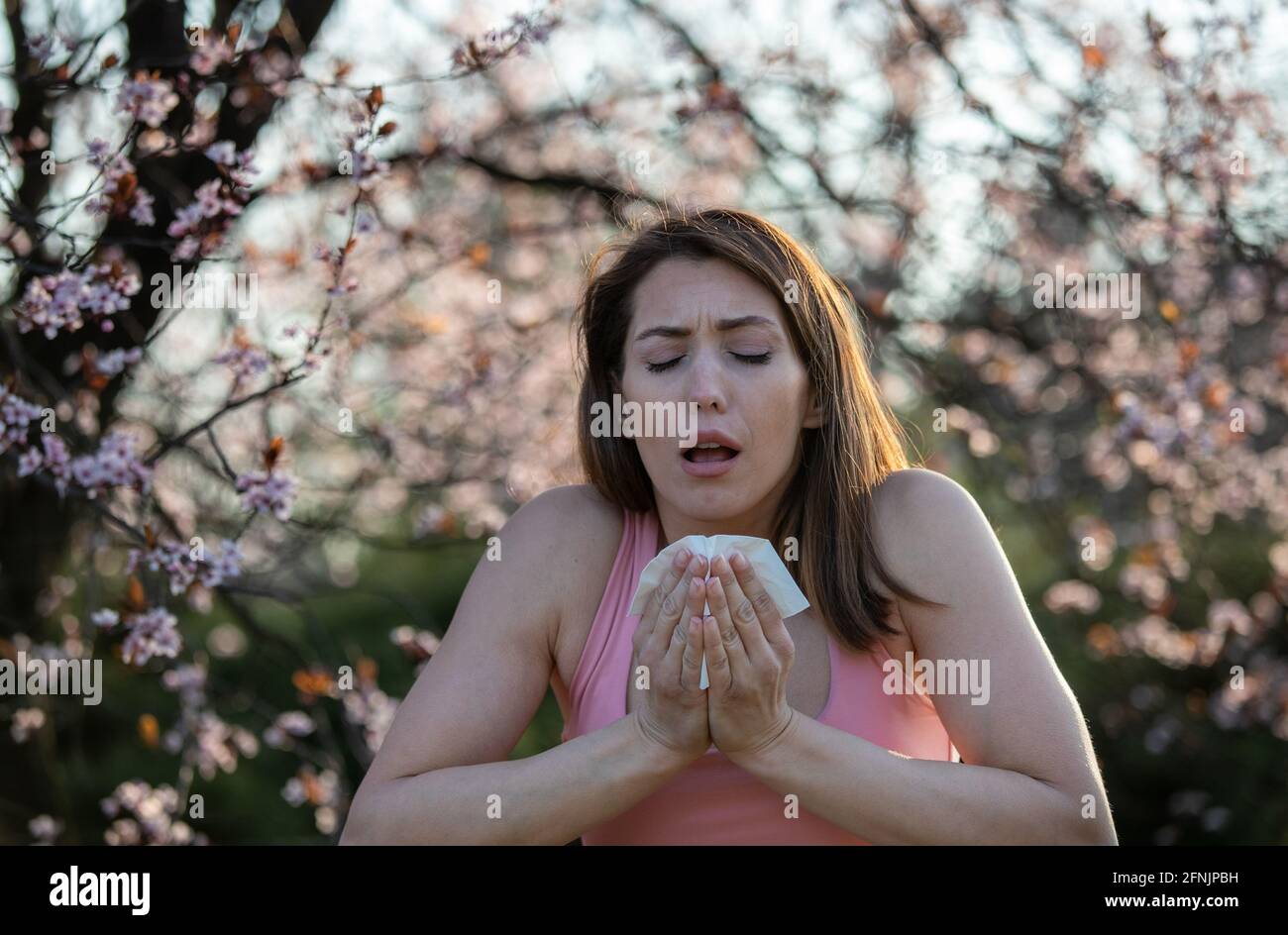 Pretty young woman sneezing in front of blooming tree. Spring allergy attack concept Stock Photo ...