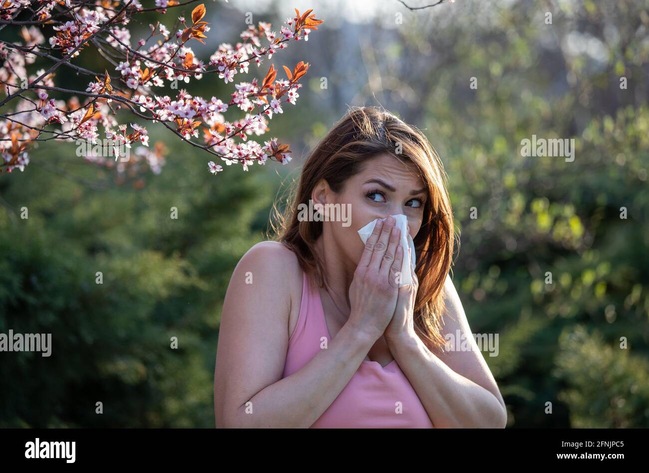 Pretty young girl blowing nose in front of blooming tree. Spring pollen allergy attack concept ...