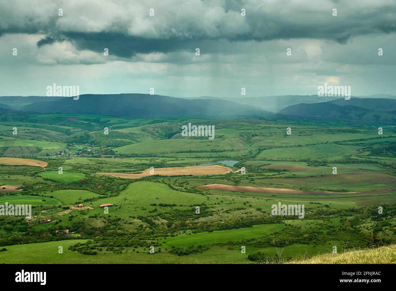 A mountain village in spring, lush green fields and trees, hills and ...