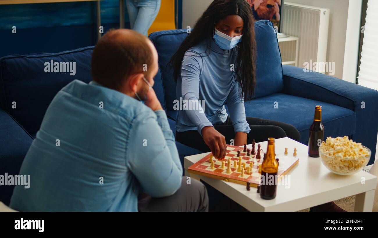 Multiethnic friends playing chess in home living room talking keeping ...